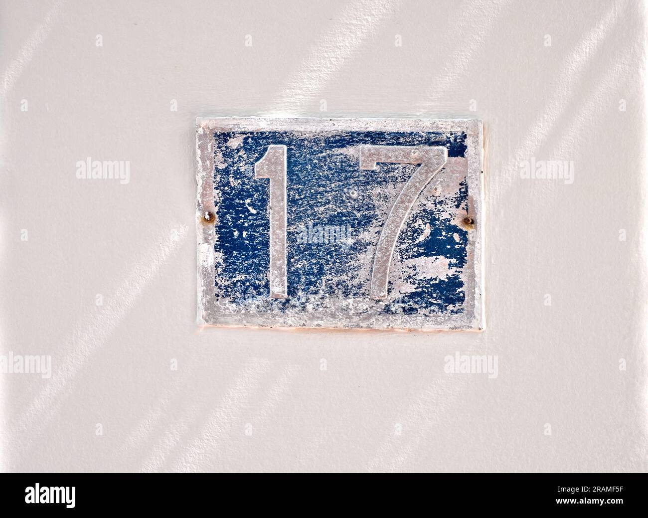 Seventeen, number 17, blue plate on white wall with sunshine and shade ...