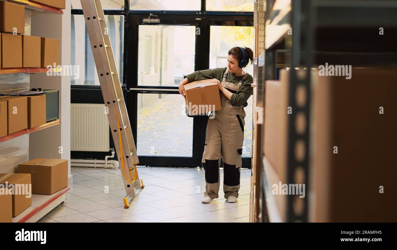 Supervisor carrying cargo boxes in depot, listening music on headphones ...
