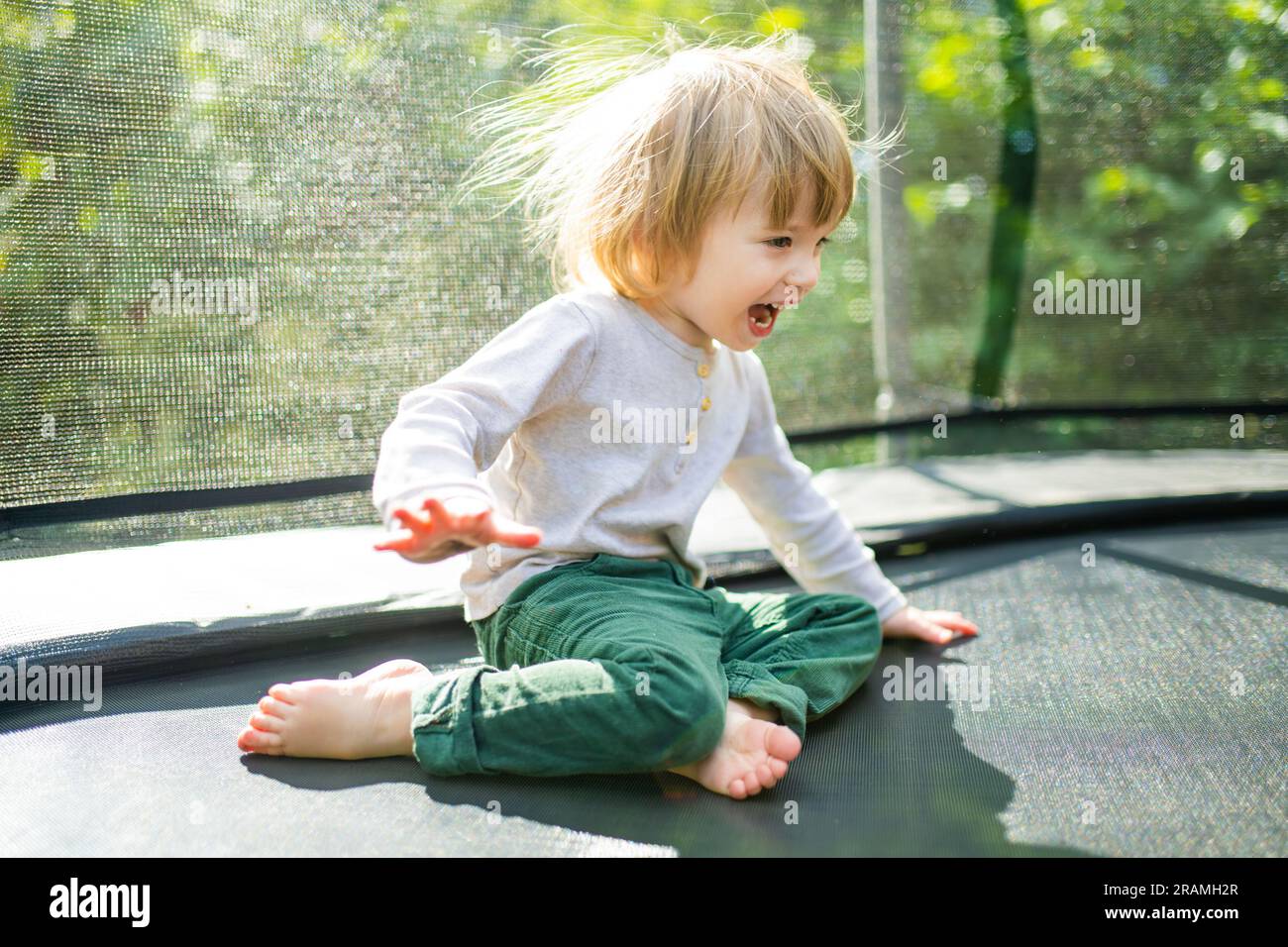Cute toddler boy jumping on a trampoline in a backyard on warm and ...