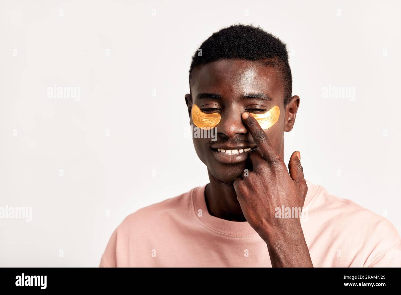 African millennial guy practicing skincare and grooming with under eye ...