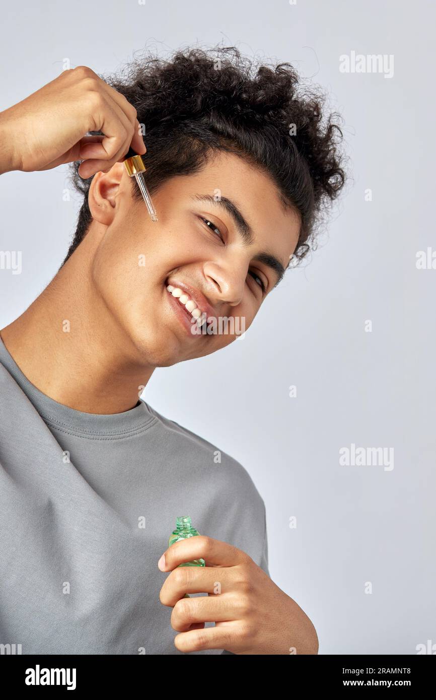 Young guy with black curly hair moisturizing his skin with a facial oil ...