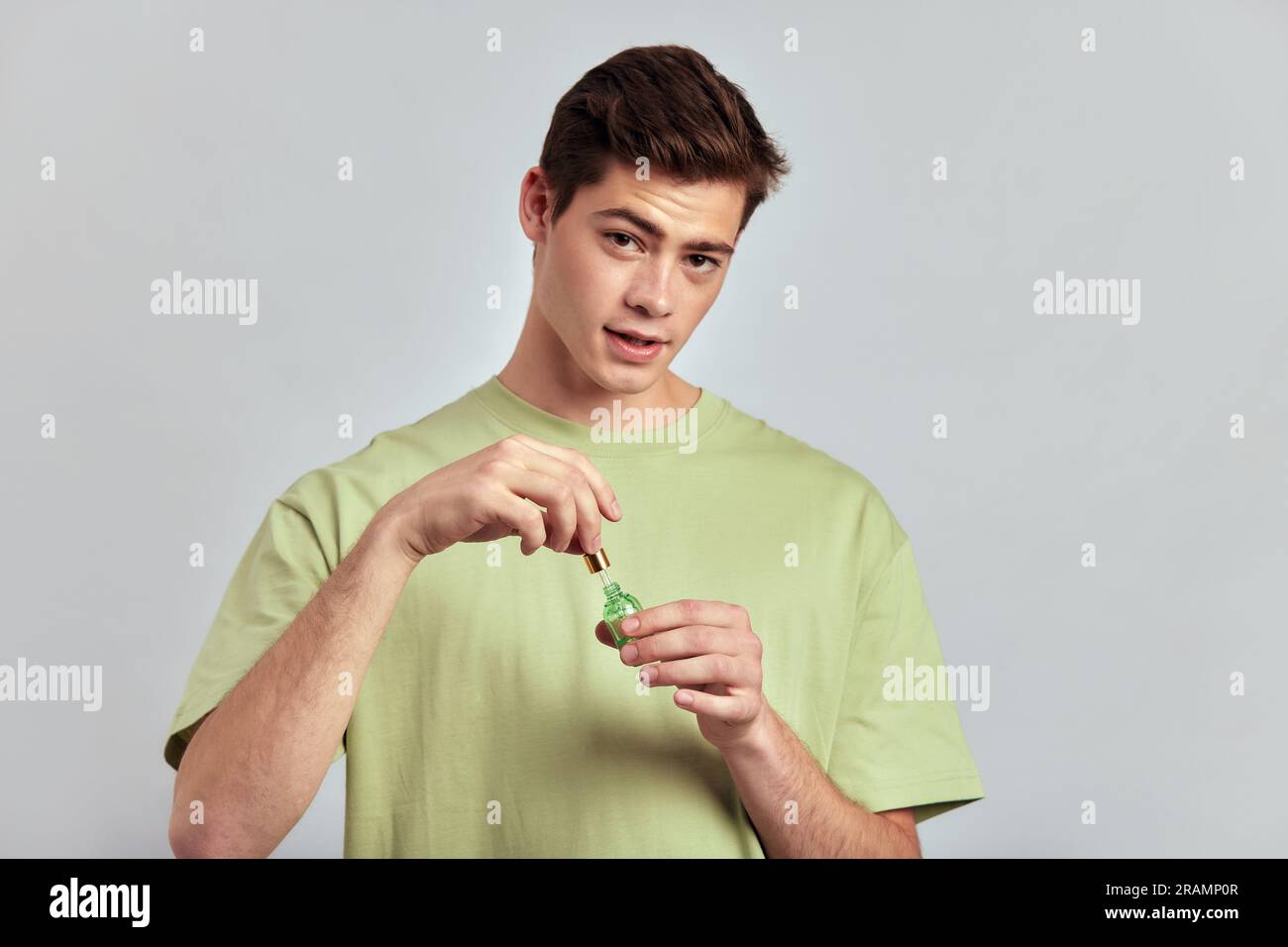 Young smiling guy moisturizing his skin with a facial oil in anti-aging ...