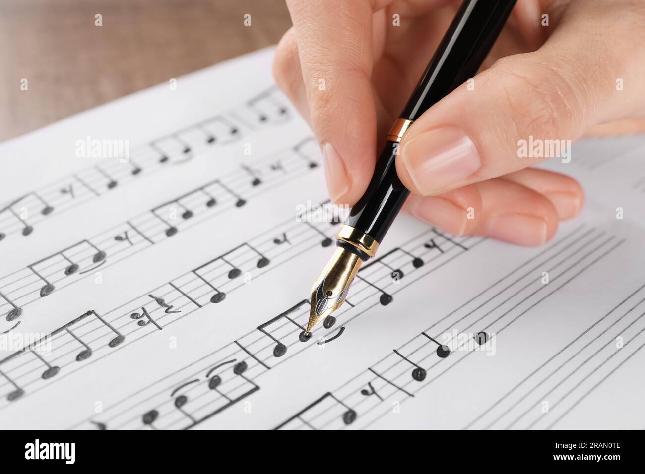 Woman writing musical notes with fountain pen on sheet of paper ...