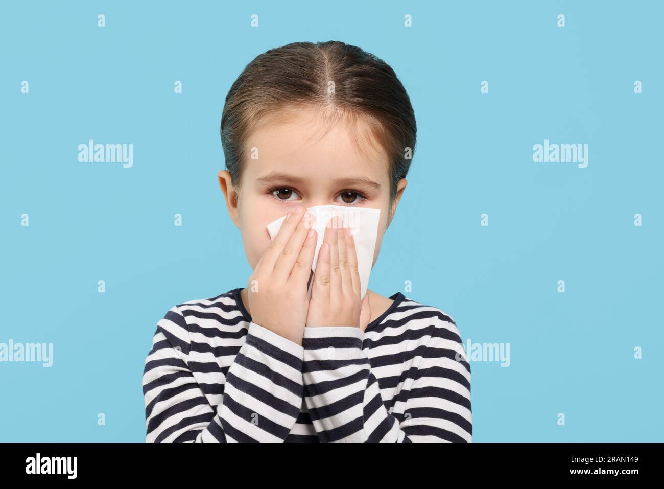 Girl blowing nose in tissue on light blue background. Cold symptoms ...
