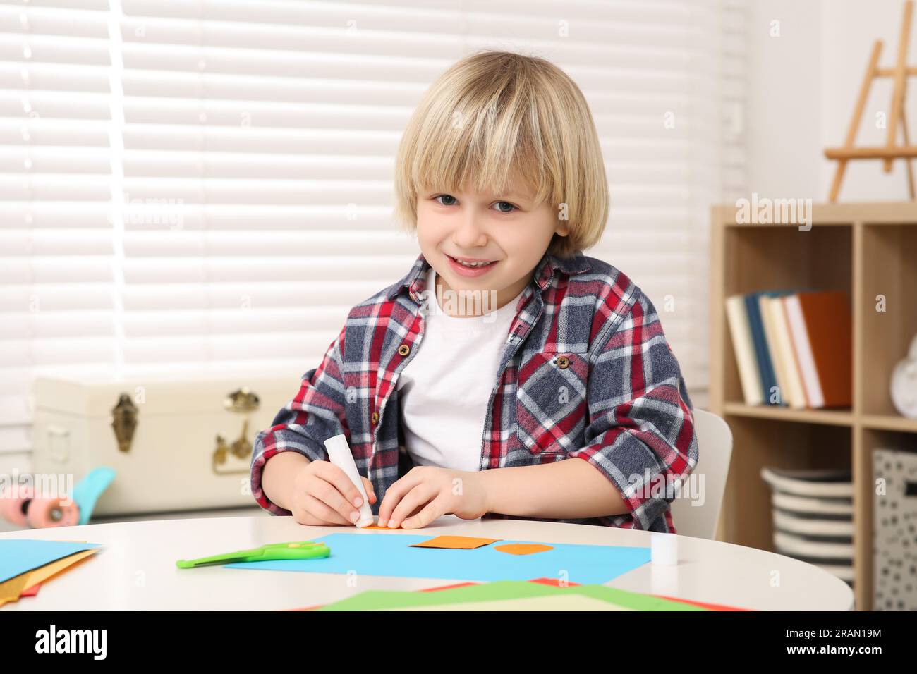 Cute little boy using glue stick at desk in room. Home workplace Stock ...