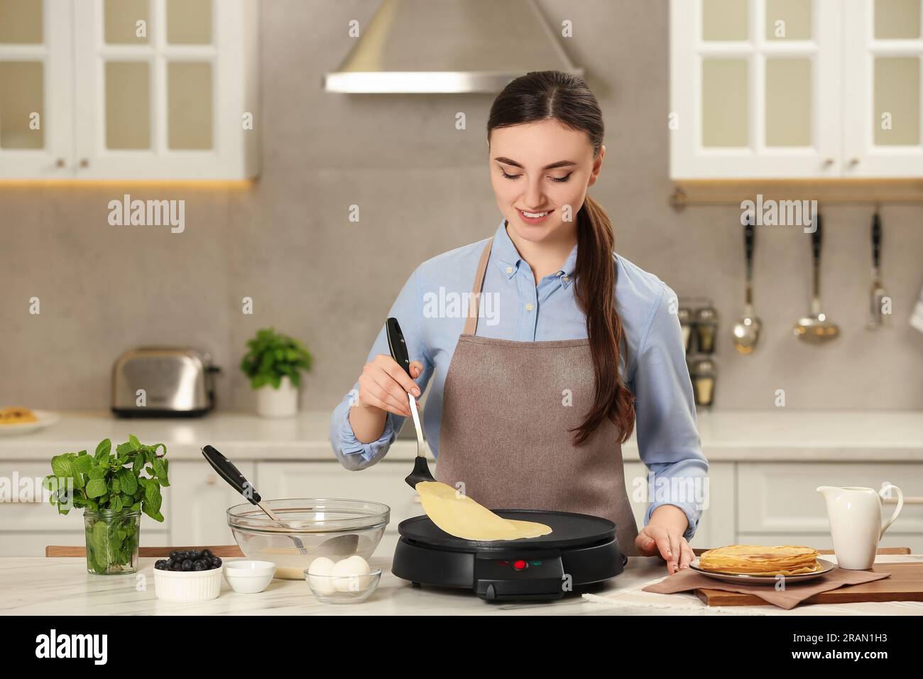 Happy woman cooking delicious crepe on electric maker at white marble ...