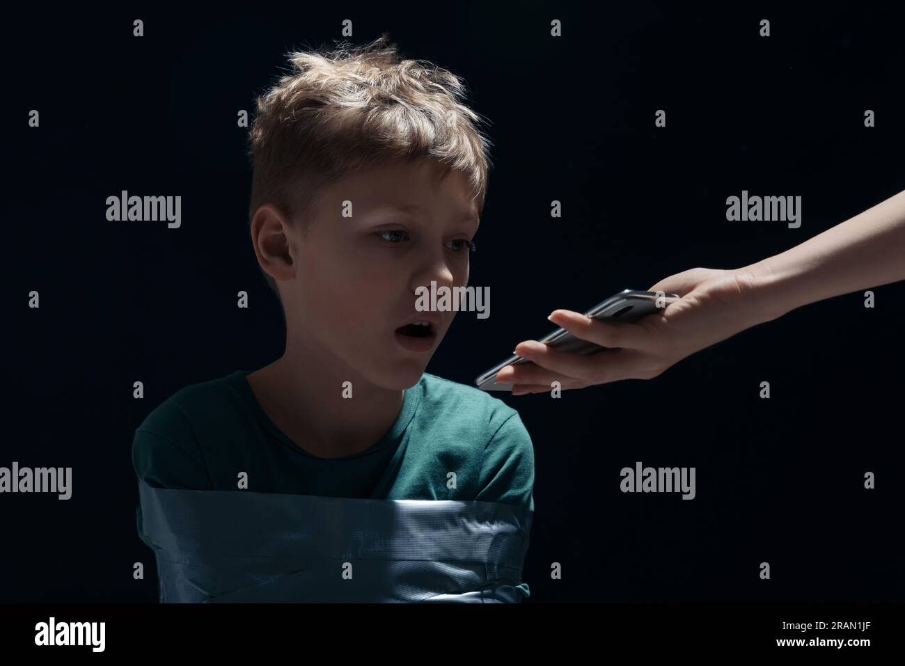 Kidnapper with phone near little boy taken hostage on dark background ...