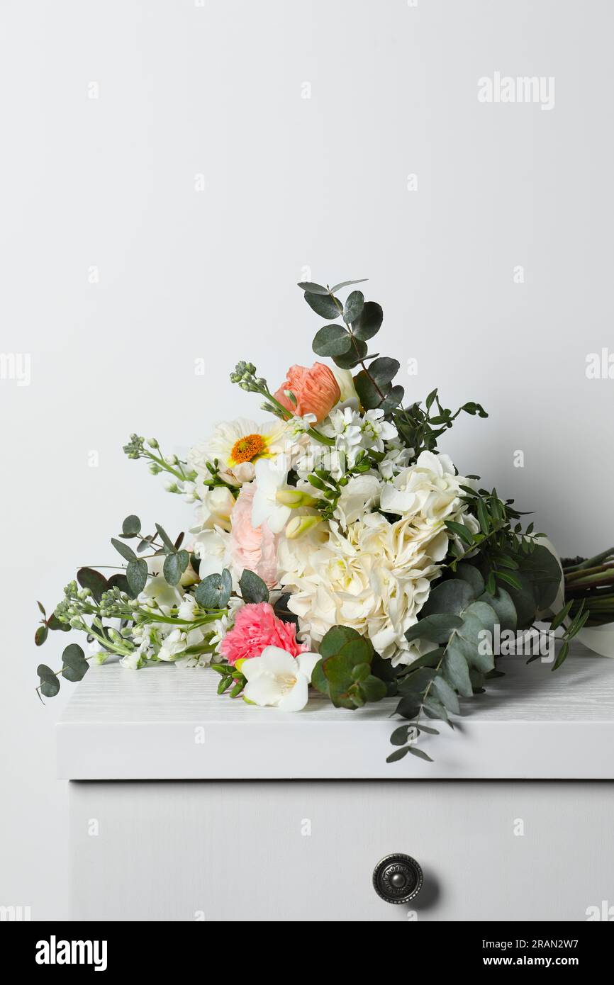 Bouquet with beautiful flowers on chest of drawers near white wall ...