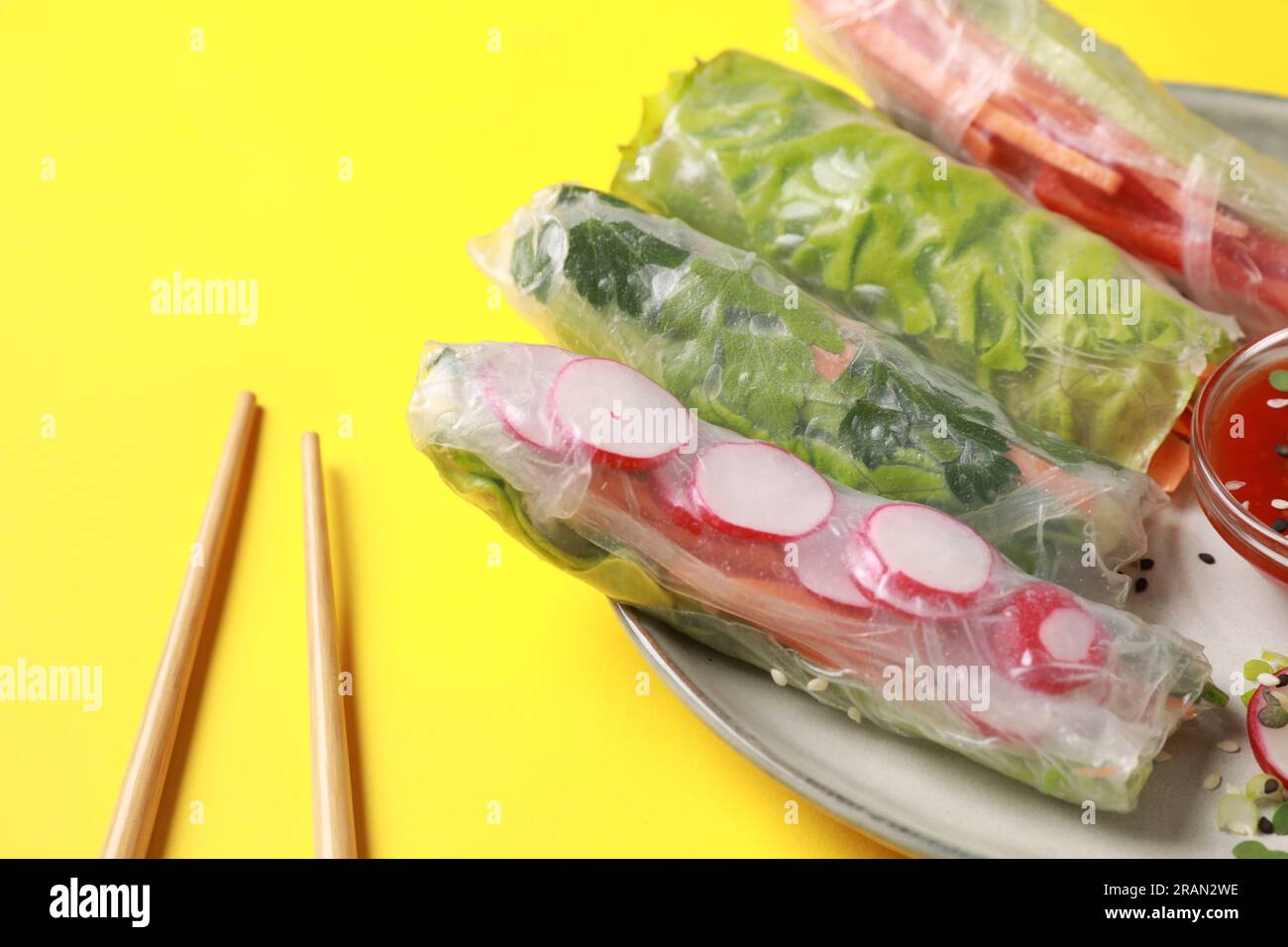 Delicious spring rolls and chopsticks on yellow background, closeup ...