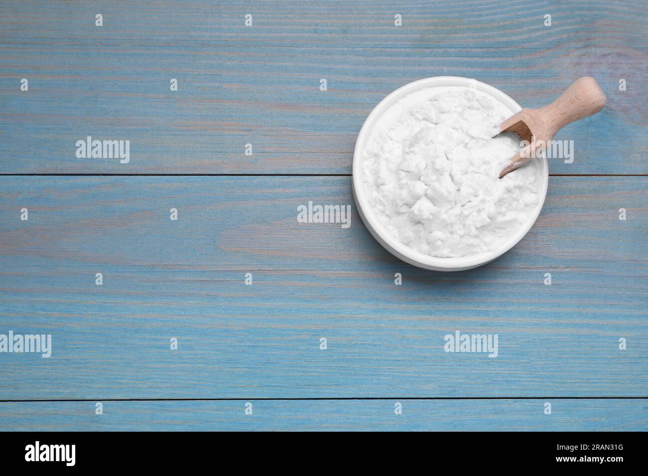 Bowl and scoop of natural starch on light blue wooden table, top view ...