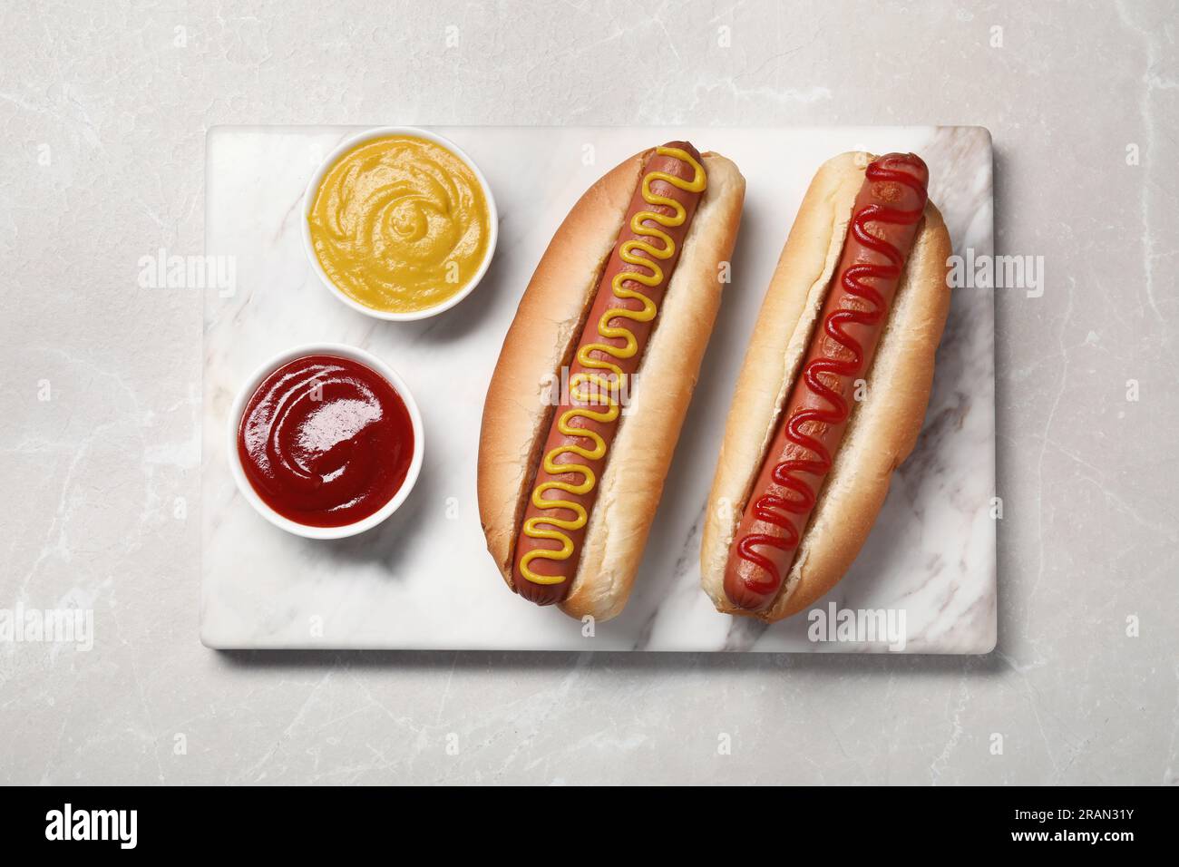 Fresh delicious hot dogs with sauces on light grey marble table, top ...