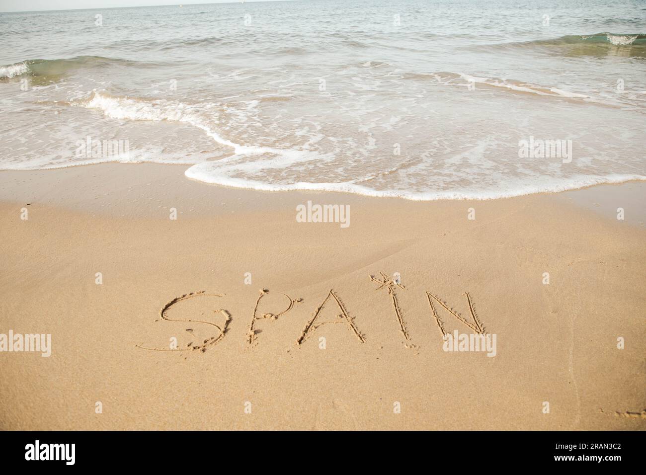 Spain lettering on the beach with wave and clear blue sea Stock Photo ...