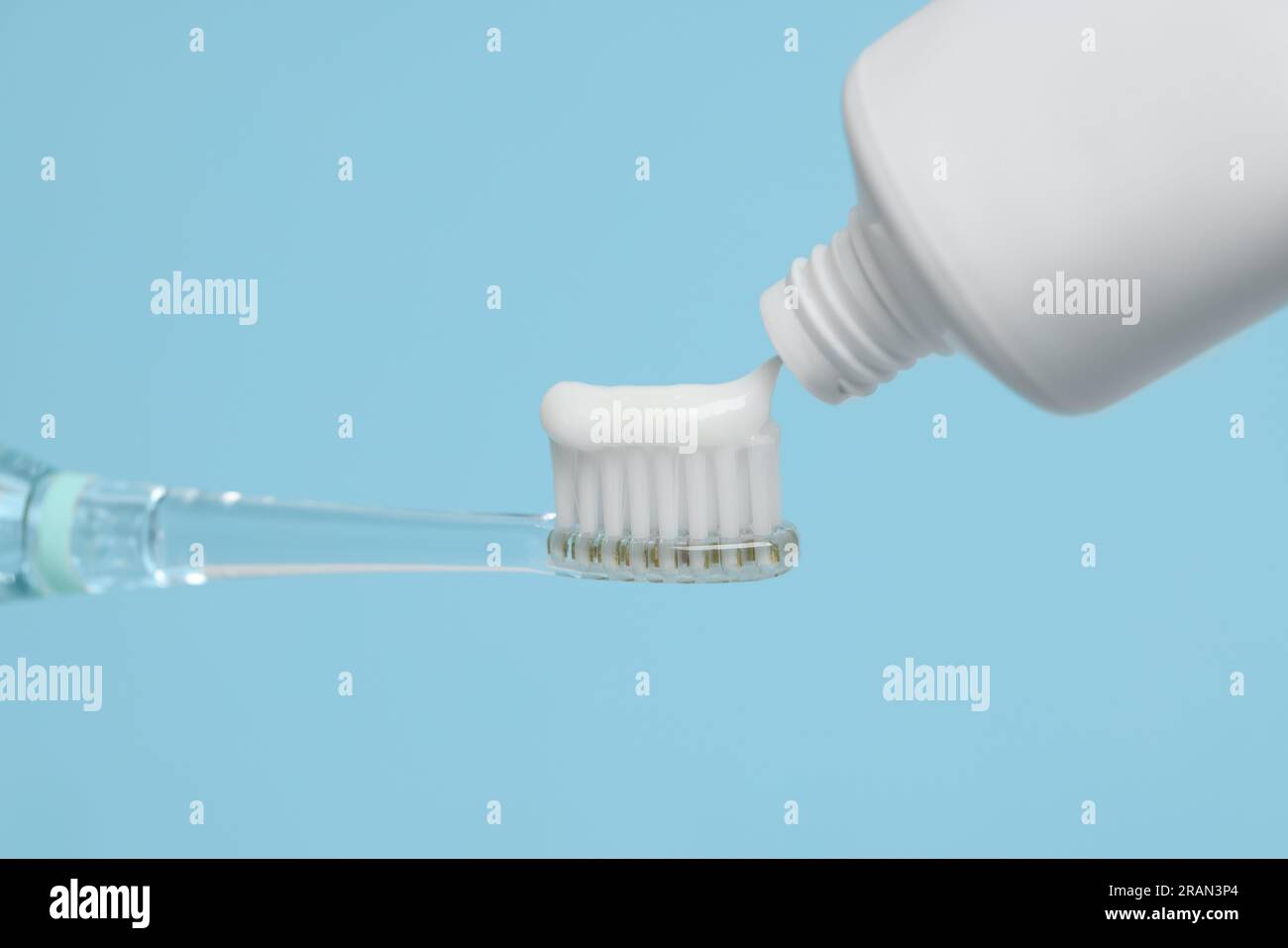 Squeezing toothpaste onto electric toothbrush on light blue background ...