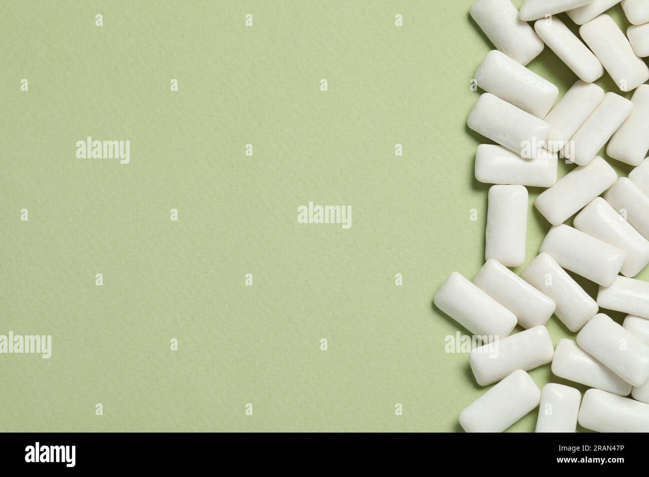 Tasty white chewing gums on light green background, flat lay. Space for ...