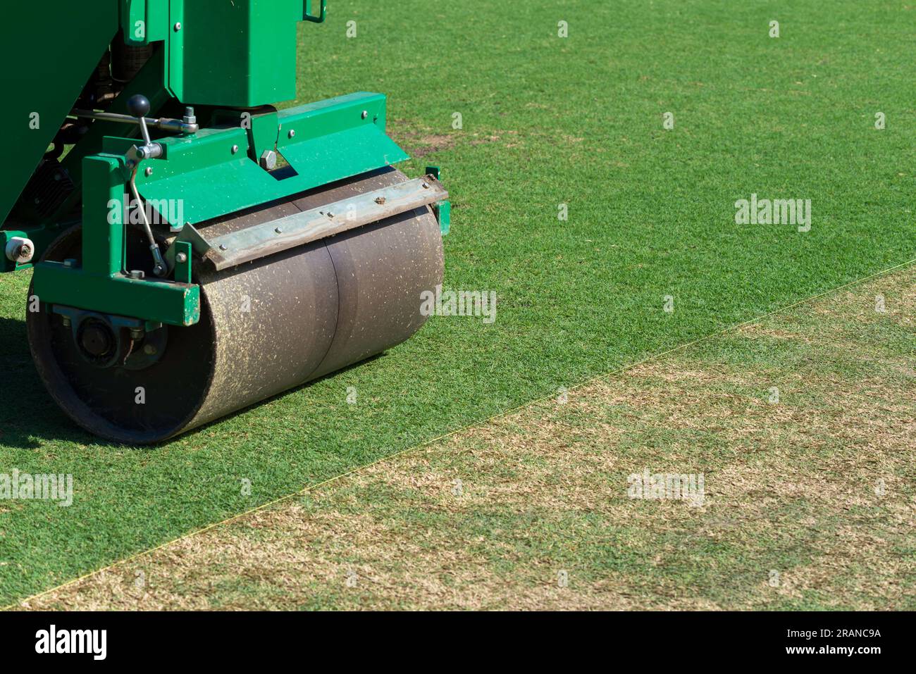 A mechanised heavy pitch roller parked beside a cricket pitch on a ...