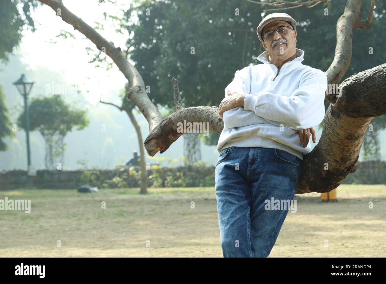 Healthy Indian cheerful old man in park standing beside tree having ...