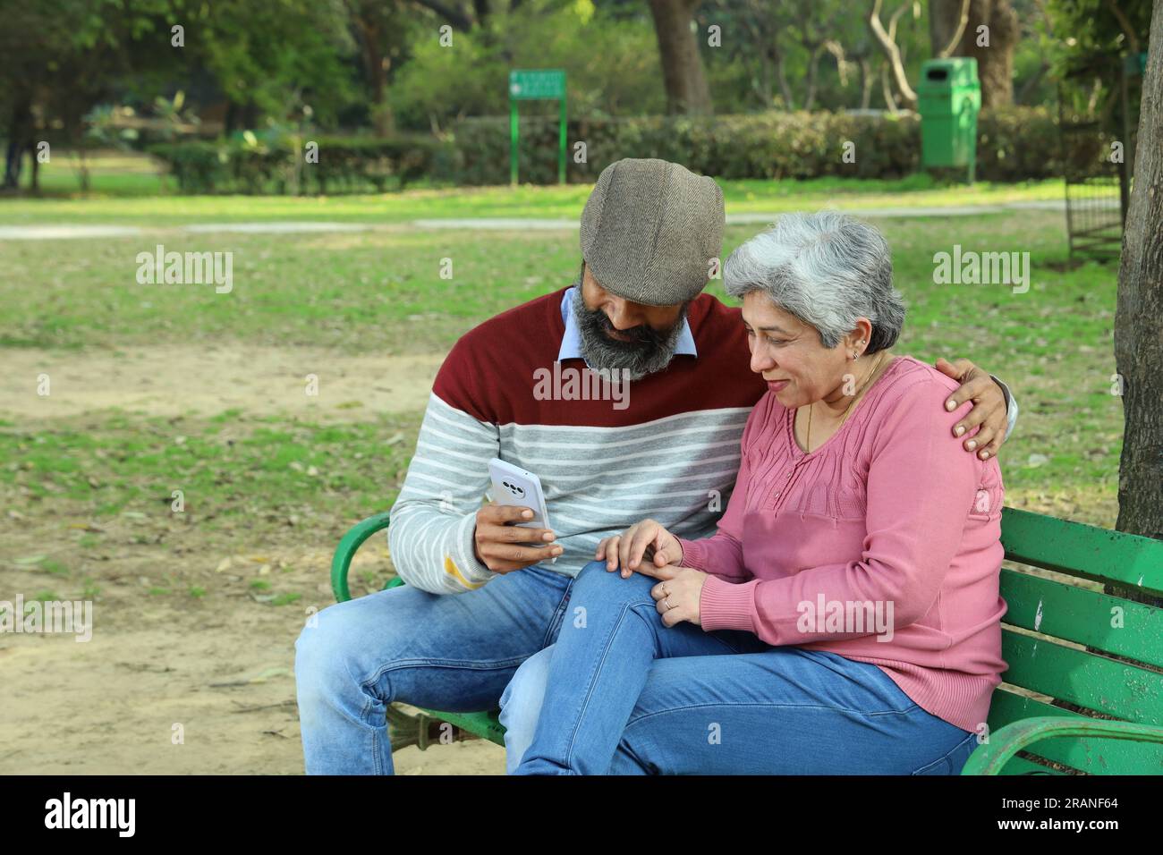 Old age couple sitting on the bench in a lush green serene environment ...