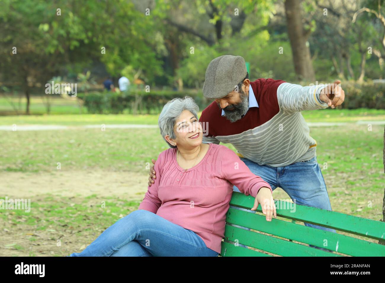 Old age couple sitting on the bench in a lush green serene environment ...