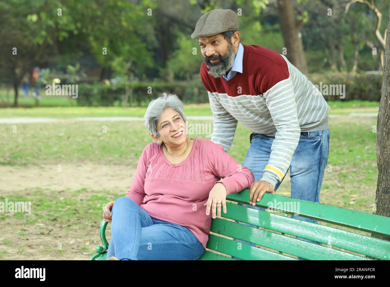 Old age couple sitting on the bench in a lush green serene environment ...