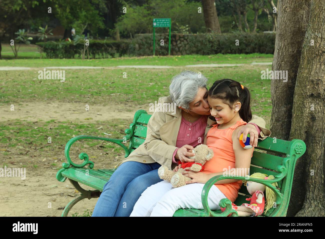 Mid Aged Mom And Daughter Sitting Outdoors In Lush Green Park In A