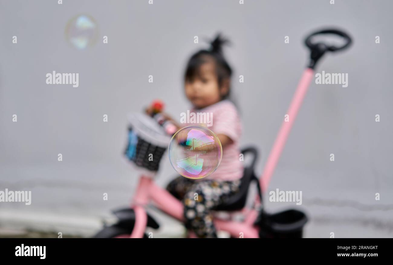 A bubble floating in front of a blurred toddler, on a bicycle, concept ...