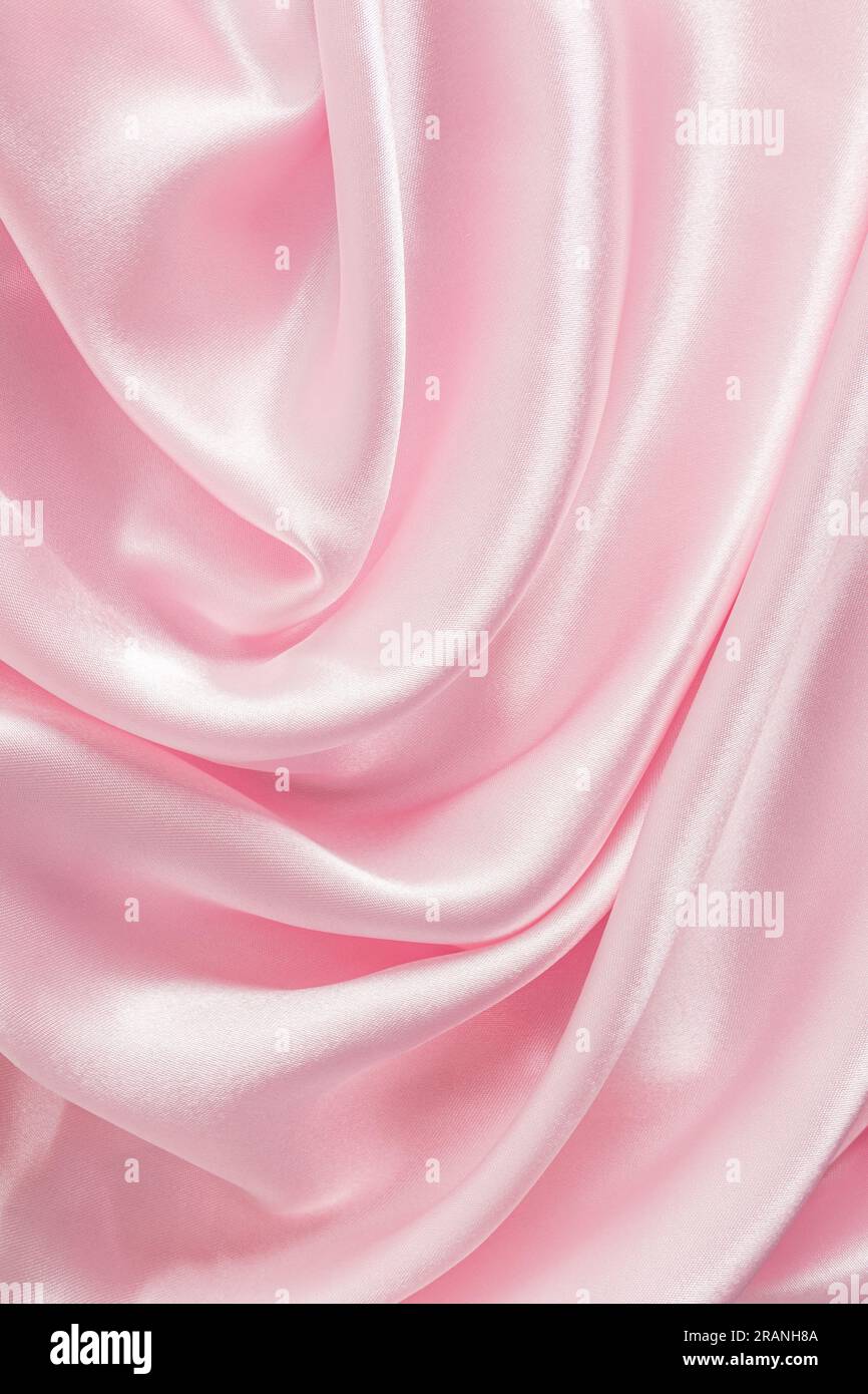 The delicate texture of the waves of pink silk satin fabric. Vertical ...