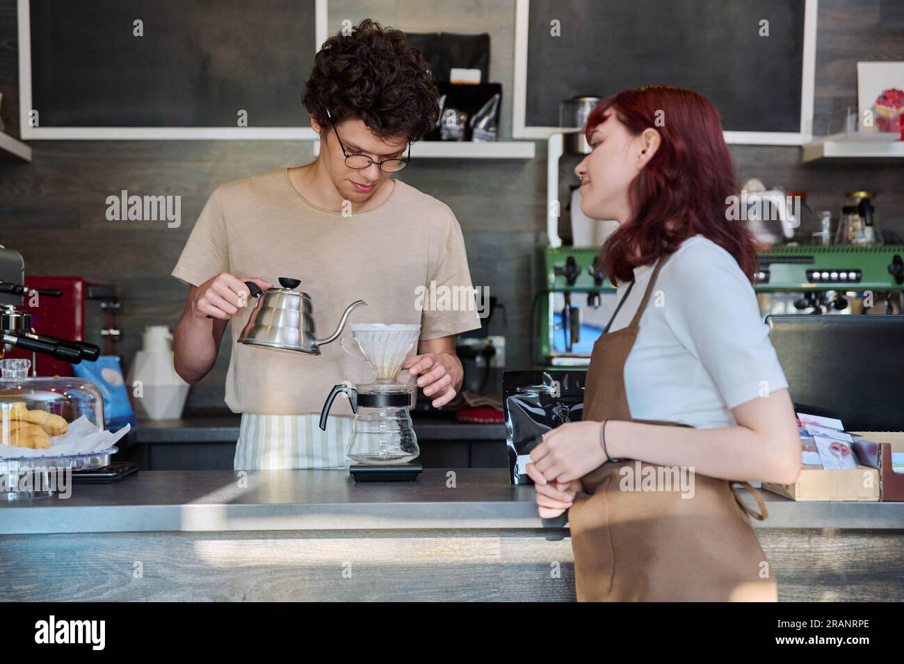 Young coffee shop workers talking, standing in front of counter in ...