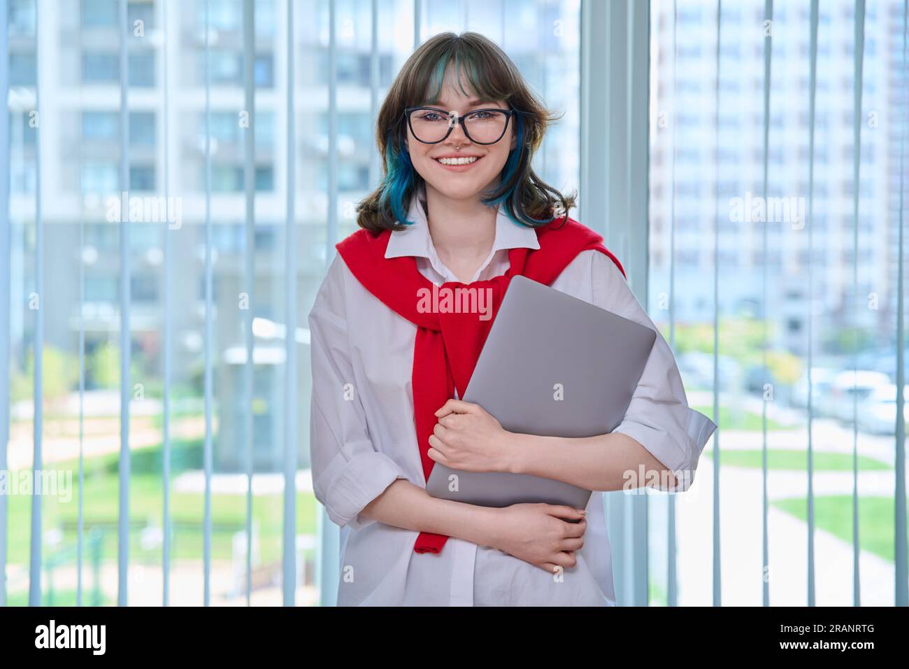 Smiling trendy female student looking at camera, holding laptop in ...
