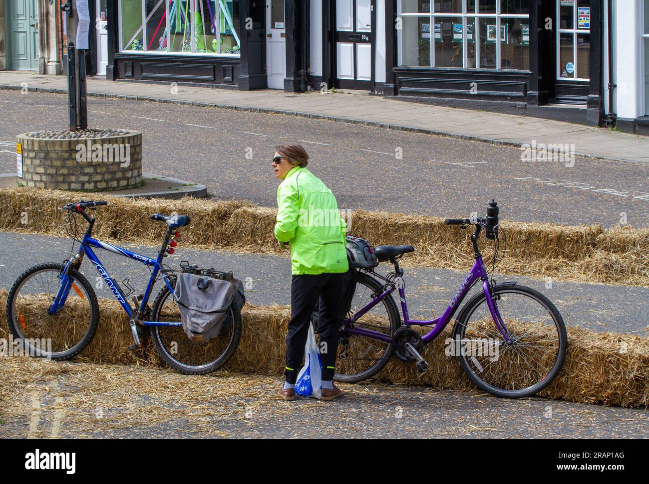 Woman cyclist with shopping in a plastic bag at her feet looks slightly ...