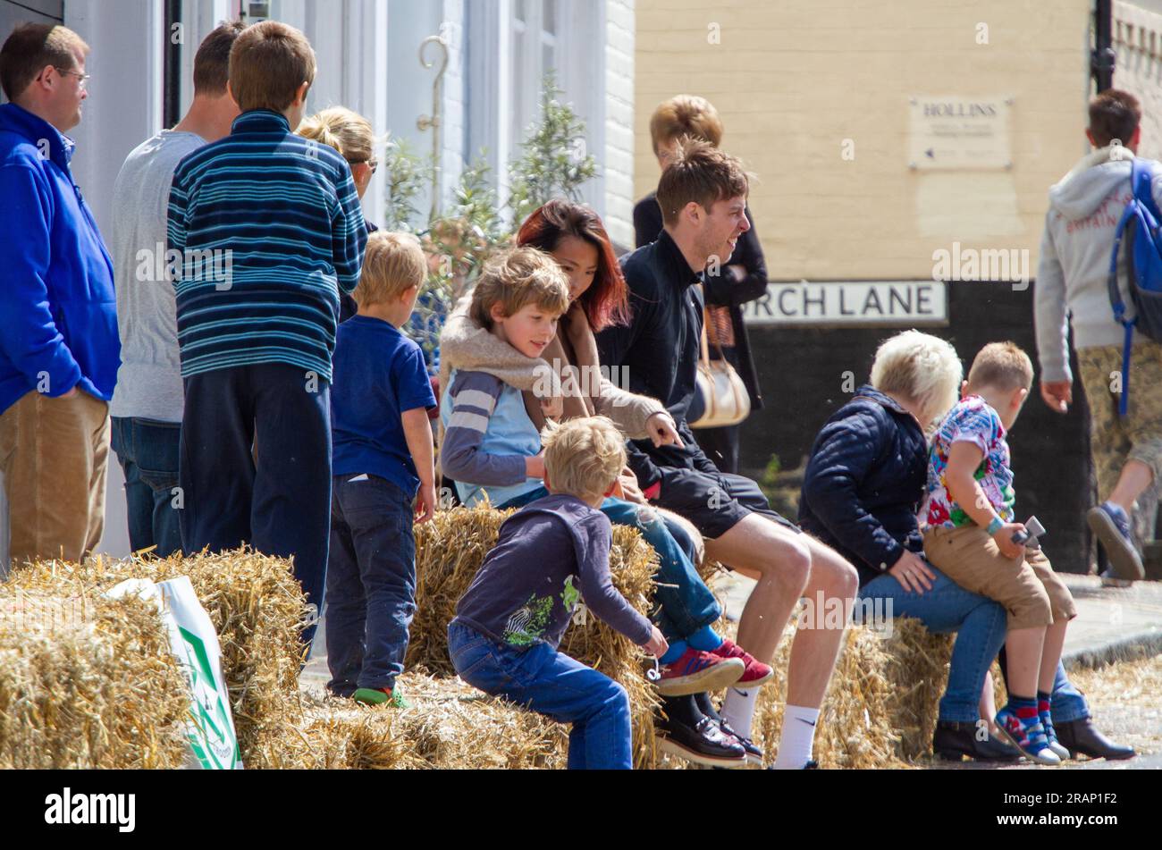 Adult and small boys seated on straw bales at the side of the road to ...