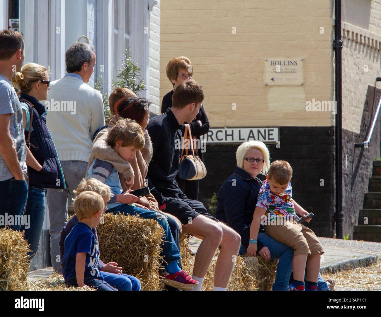 Adult and small boys seated on straw bales at the side of the road to ...