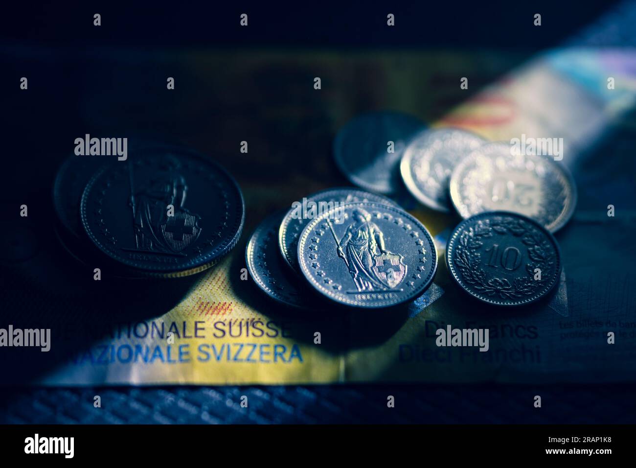 Several Swiss franc coins resting on an old banknote hit by a ray of ...