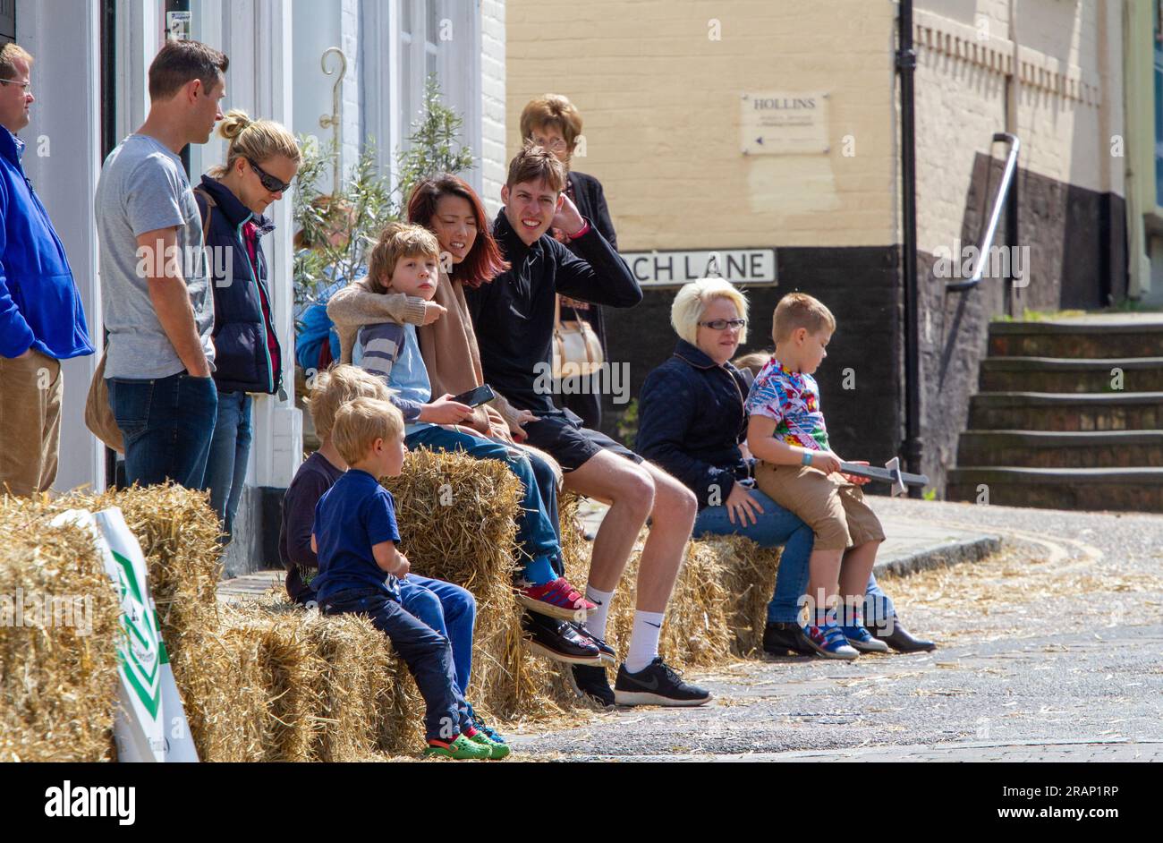 Adult and small boys seated on straw bales at the side of the road to ...