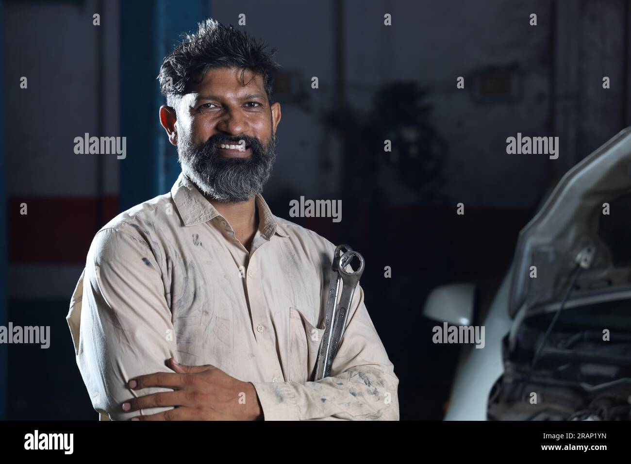 Bearded Indian car mechanic smiling while examining car. Car specialist ...