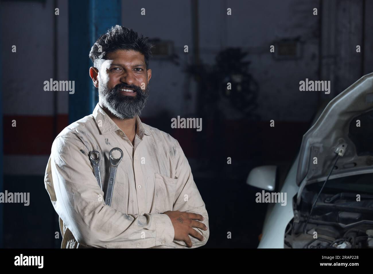Bearded Indian car mechanic smiling while examining car. Car specialist ...
