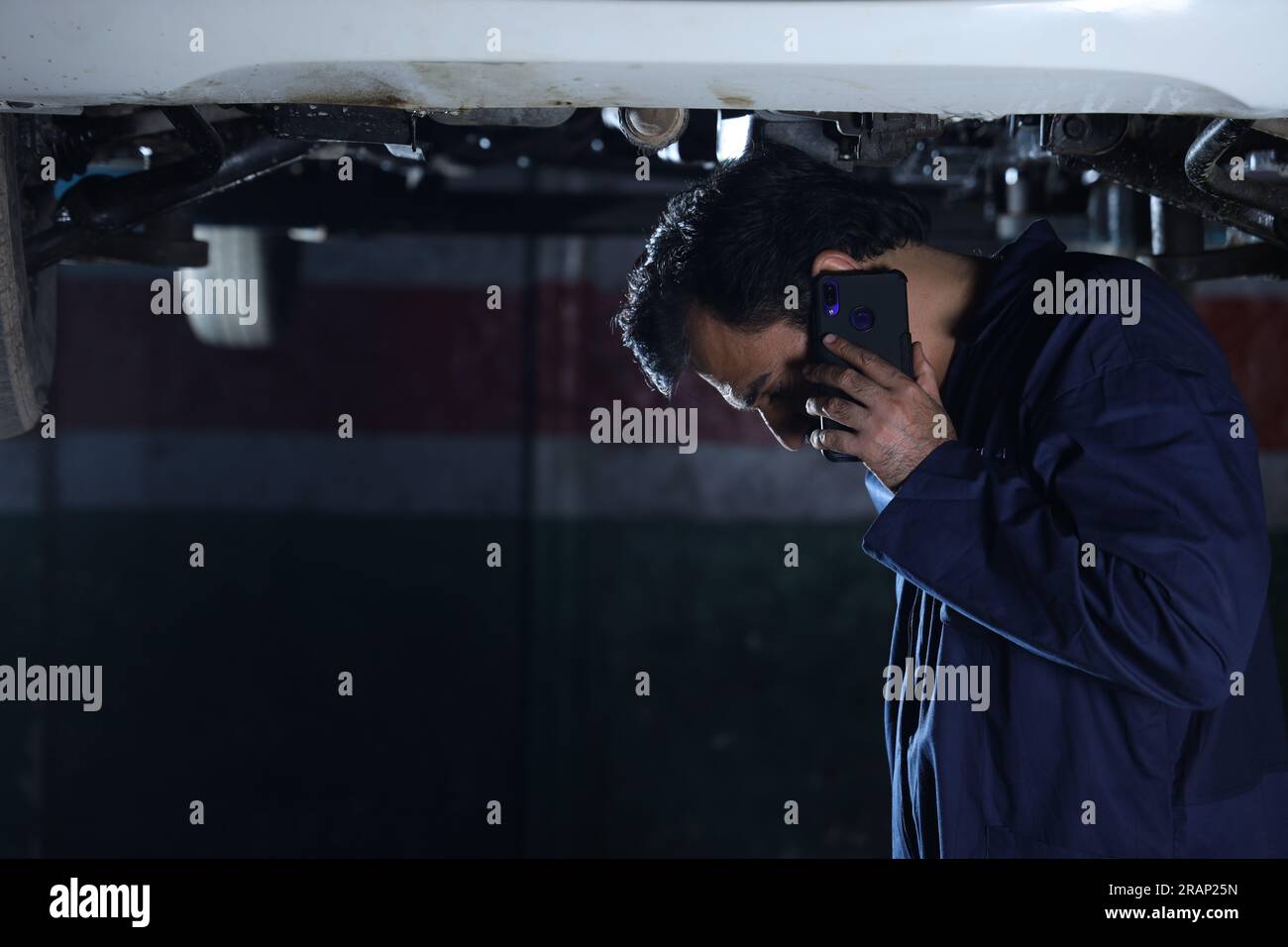 Mechanic working under lifted car in workshop. Specialist is examining ...