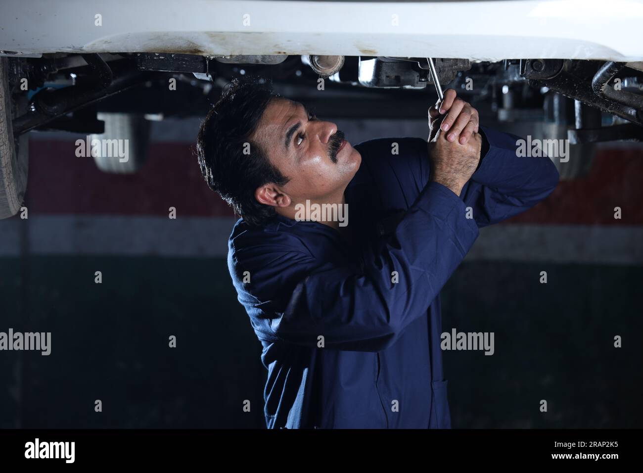 Mechanic working under lifted car in workshop. Specialist is examining ...