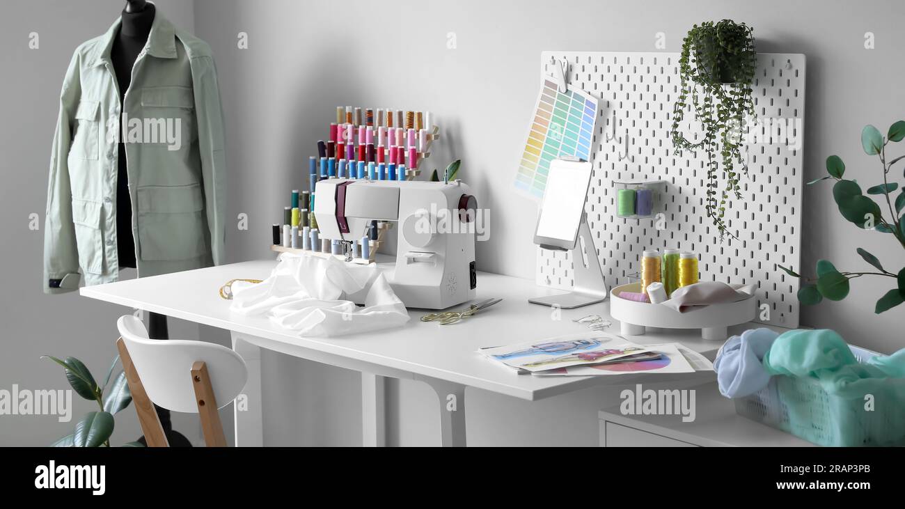 Tailor's workplace with sewing machine, pegboard and tablet computer in ...