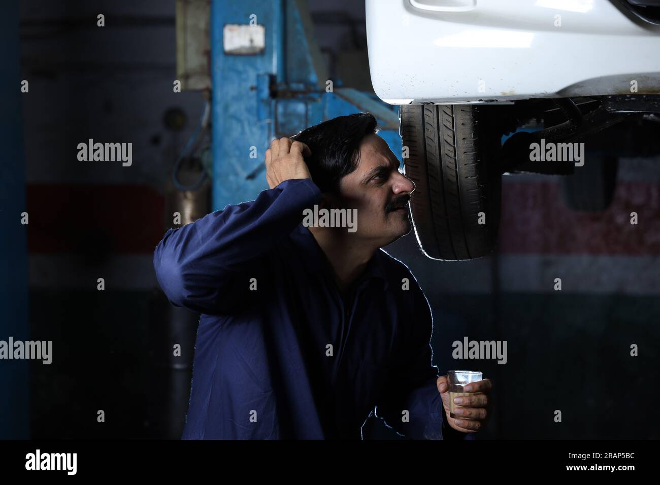 Portrait of happy car mechanic in moustache repairing and examining the ...
