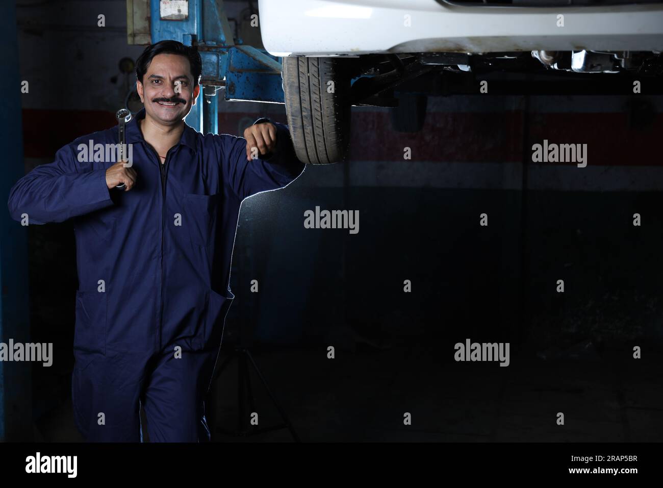 Portrait of a happy car mechanic in moustache standing beside car in ...