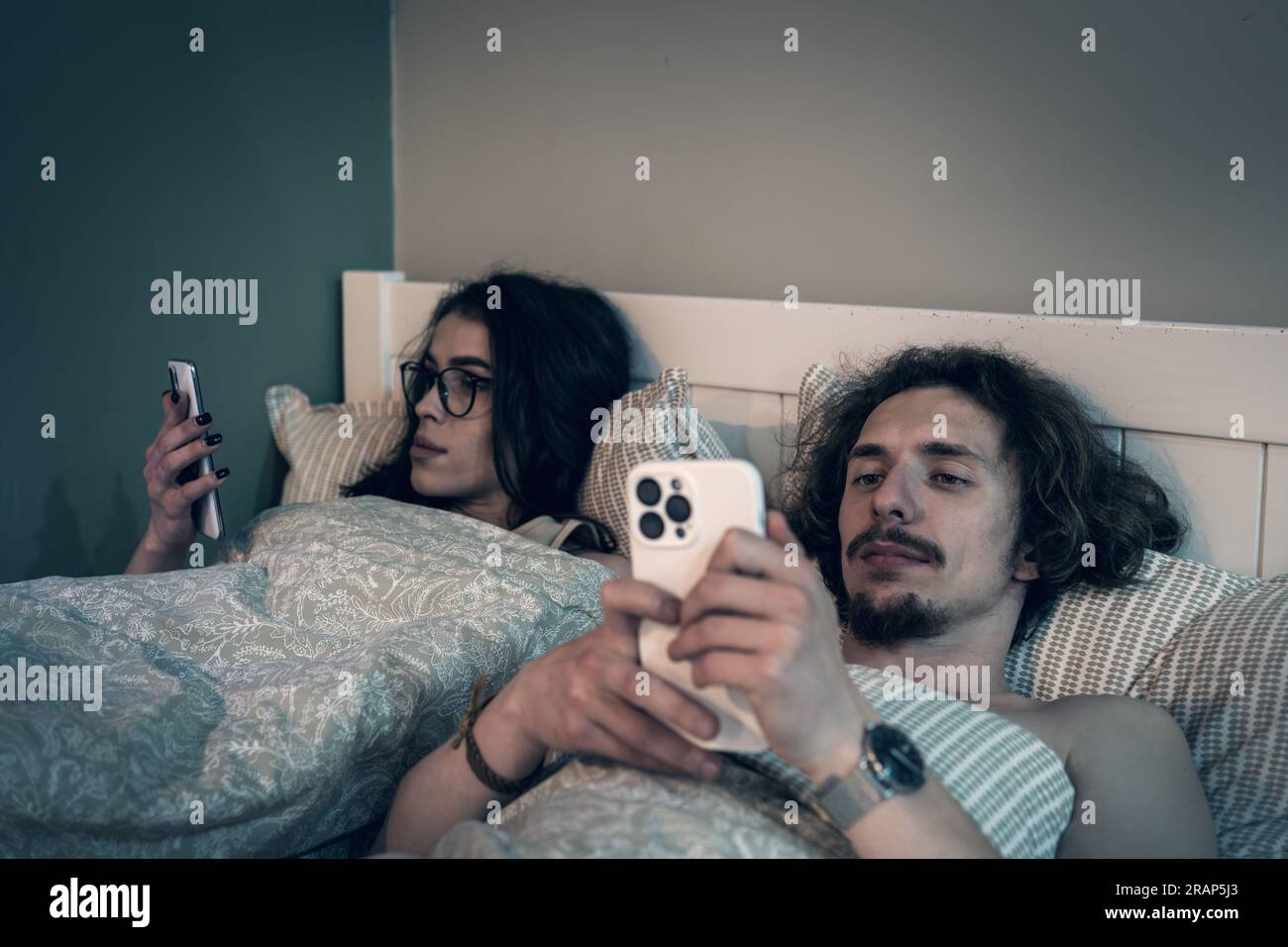 Married couple lying in bed together but each of partners use ...