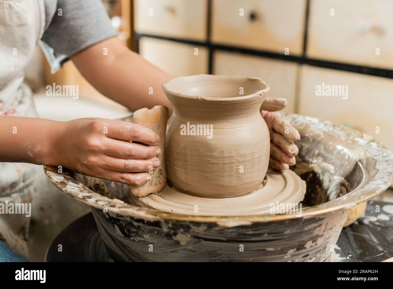 Cropped view of young female artisan in apron making clay vase with ...