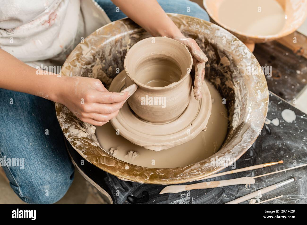 Top view of young female potter in apron making shape of clay vase with ...