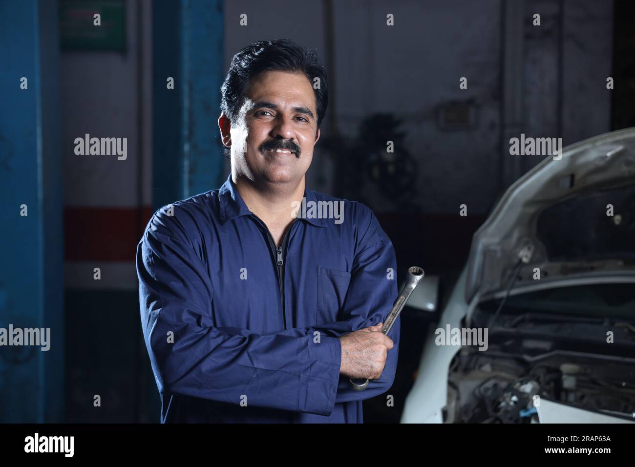 Portrait of a happy car mechanic in moustache standing beside car in ...
