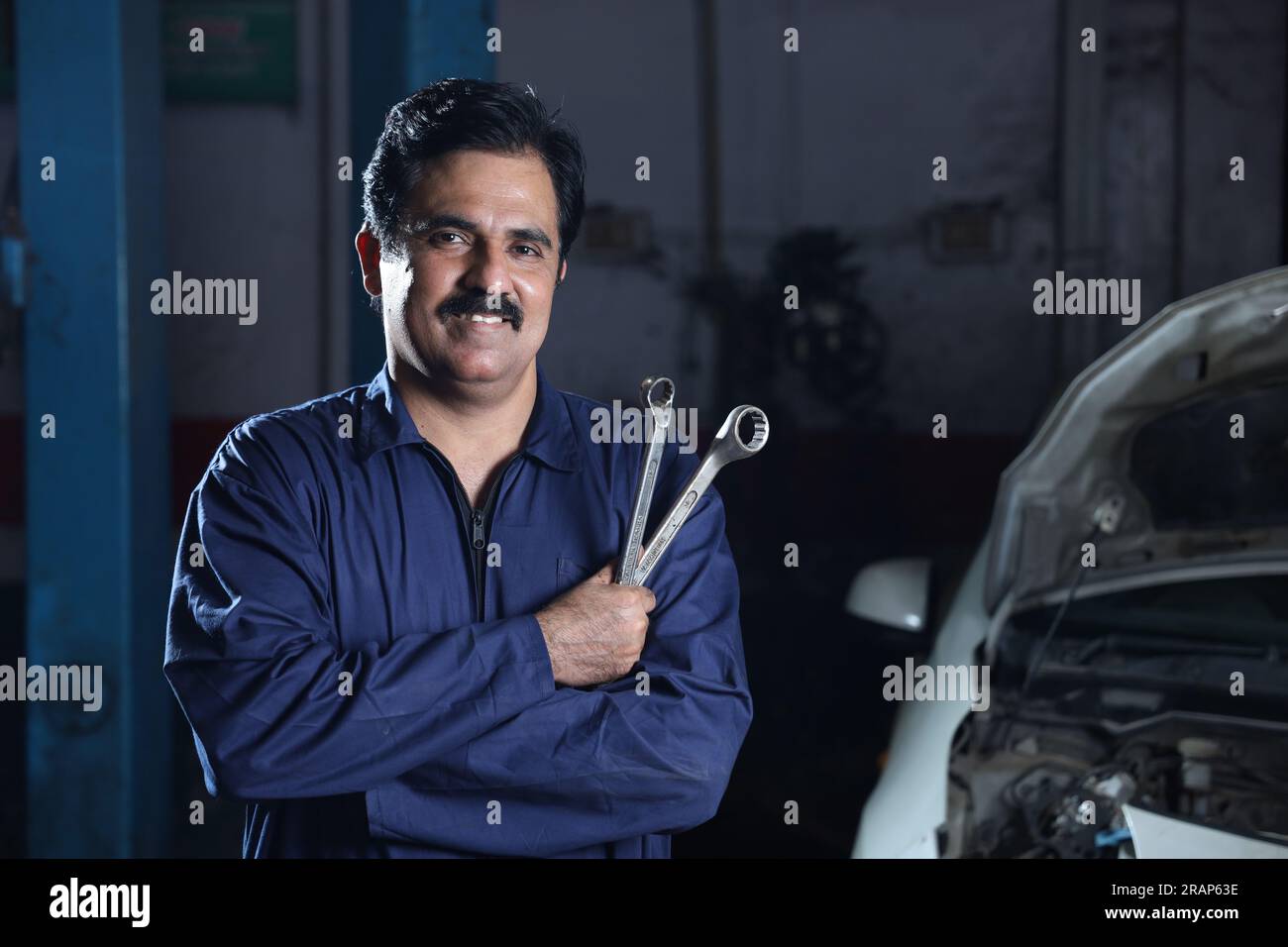 Portrait of a happy car mechanic in moustache standing beside car in ...
