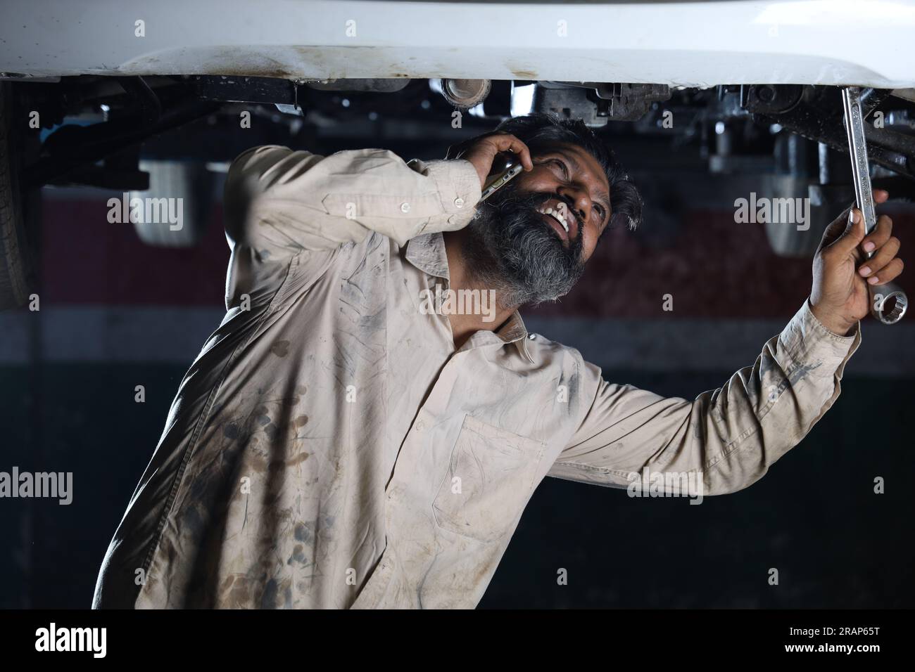 Portrait of happy car mechanic in moustache repairing and examining the ...