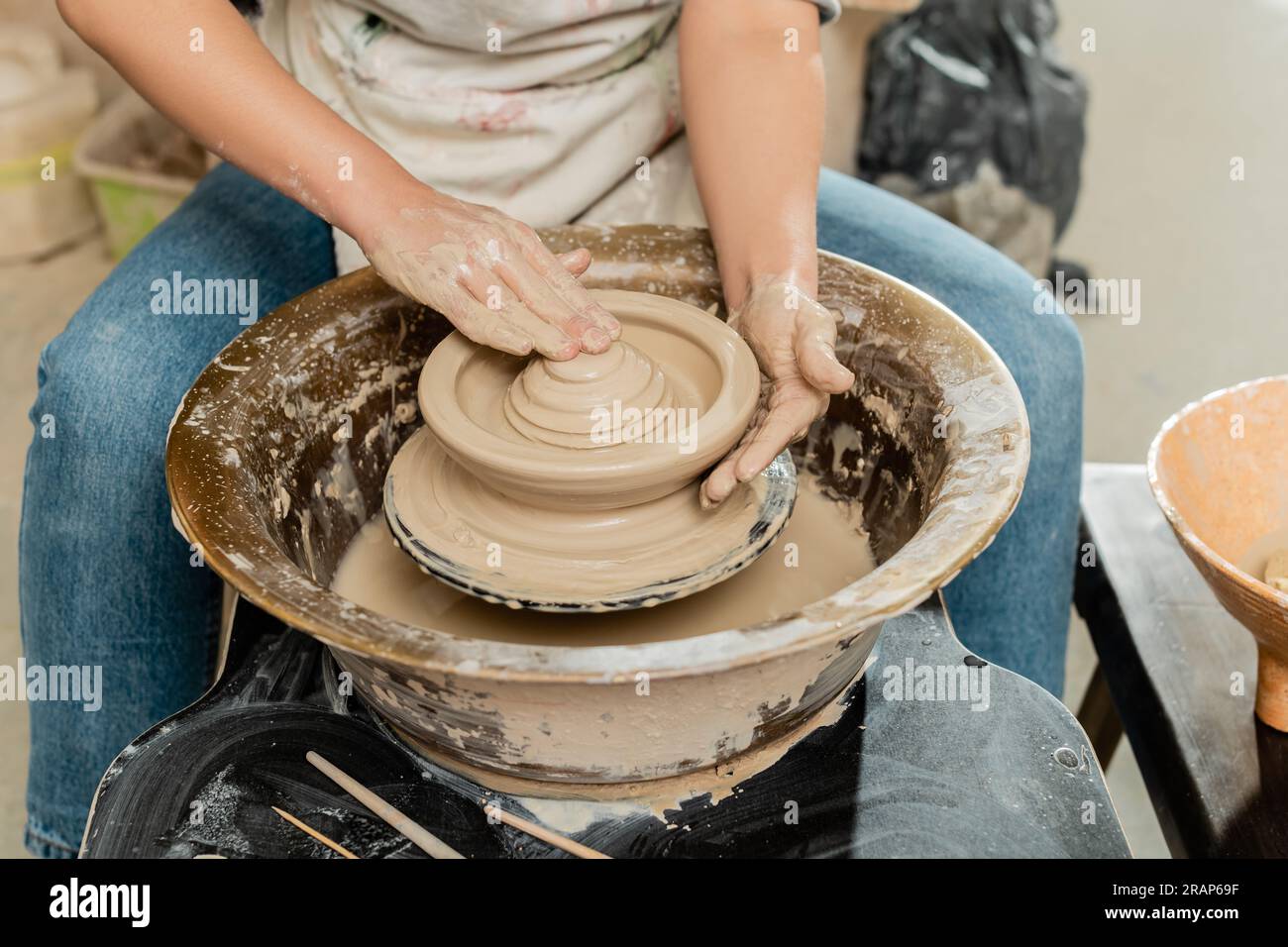 Cropped view of young female artist in apron molding clay and making ...