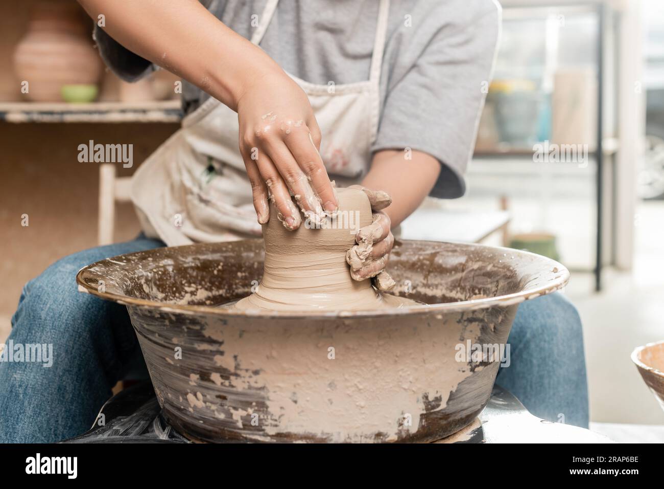 Cropped view of blurred young female artisan in apron molding clay on ...