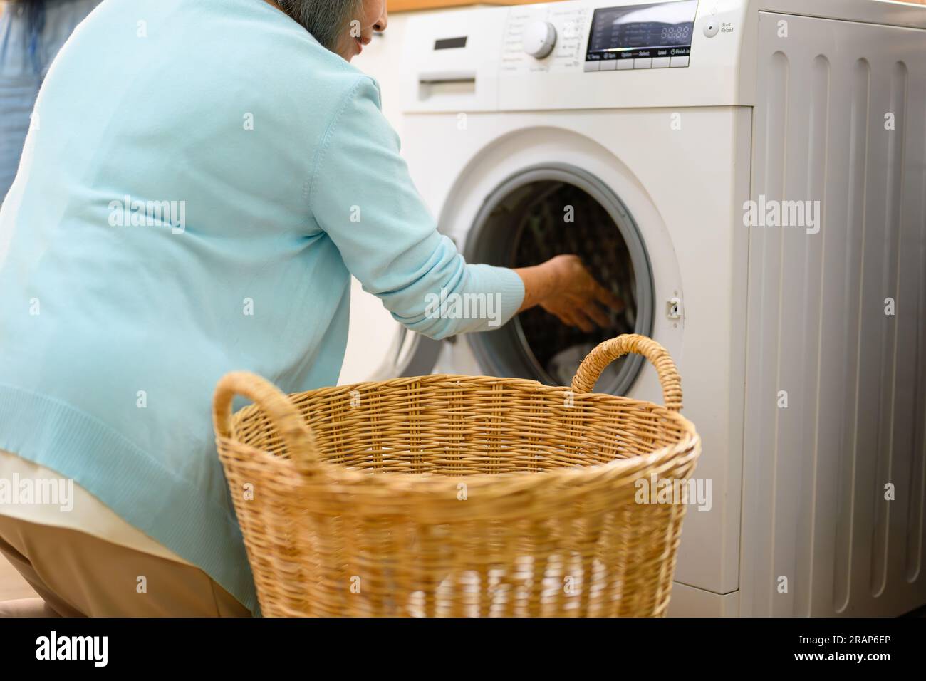 a beautiful senior woman, takes care of the laundry using a washing ...