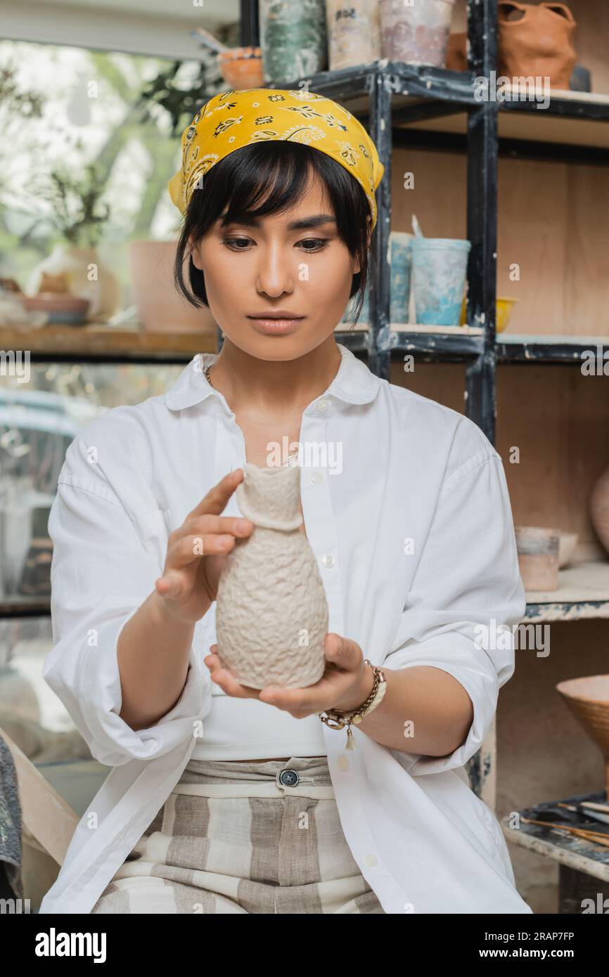 Portrait of young asian female potter in headscarf and workwear holding ...